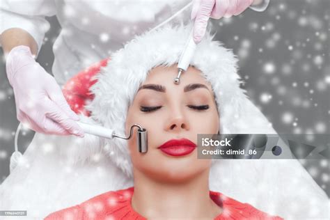 미용사들은 눈의 배경에 산타 클로스 모자를 쓴 여성의 미세 전류 치료 절차를 만듭니다 새해와 화장품 개념 크리스마스에 대한 스톡 사진 및 기타 이미지 Istock