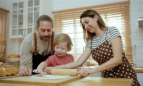 아버지와 어머니는 아기 아들이 집에 있는 부엌 카운터에서 반죽을 반죽하는 것을 가르친다 부모와 소년 아이는 실내 활동을 함께