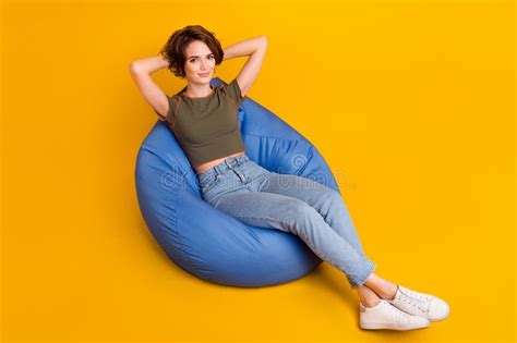 Full Length Photo Of Pretty Cute Lady Wear Khaki T Shirt Sitting Bean Bag Arms Behind Head Empty