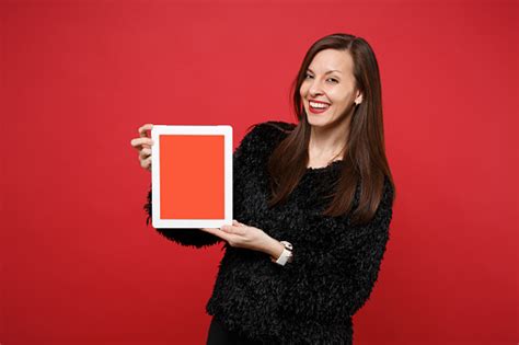 스튜디오에서 빨간 벽 배경에 고립 된 빈 빈 화면으로 태블릿 Pc 컴퓨터를 들고 검은 모피 스웨터에 밝은 젊은 여자 사람들이