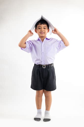 지붕처럼 머리 위로 책을 들고 있습니다 배낭 가방이 있는 태국 교복 젊은 아시아인은 하얀 배경 배너에 서 있는 귀여운 소년을 흥분시킨다 학교로 돌아 가기 6 7 살에 대한
