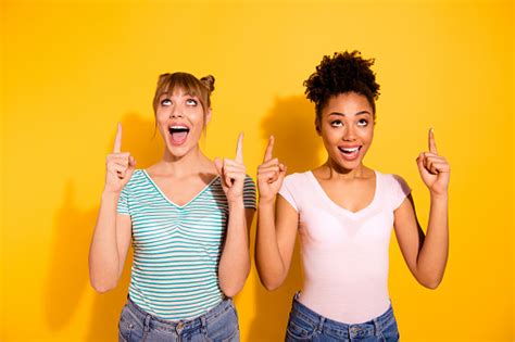 클로즈업 사진 아름 다운 두 사람 그녀의 모델 여자 다양성 인상 인덱스 손가락을 보고 빈 공간 깜짝 놀란 착용 우연한 화이트 스트라이프 티셔츠 옷 고립 된 노란 밝은 배경