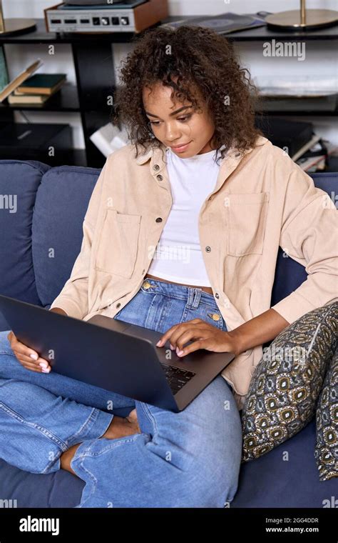 African American Female Student Sitting On Soft Sofa At Home Using Pc