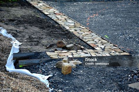 돌 포장은 두 개의 강판 연석 사이의 자갈 백필에서 방금 건조되었습니다 소박한 느낌의 사암과 탄 벽돌 조각 허브 정원의 좁은 공원 경로 토양 재배 오솔길에 대한 스톡 사진