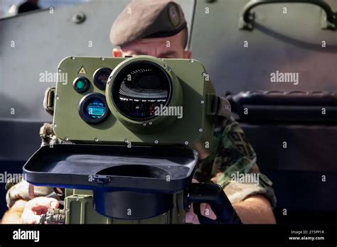 Soldier In Camouflaged Uniform Armed With Military Equipment Next To Armored Vehicle Using
