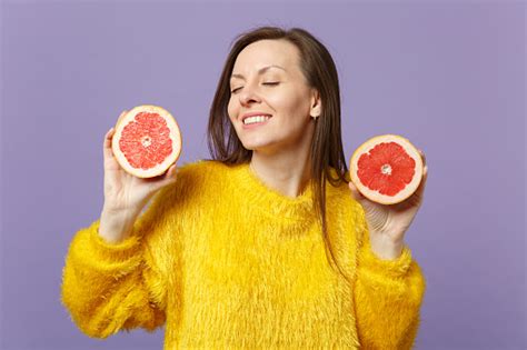 모피 스웨터에 예쁜 젊은 여 자가 보라색 파스텔 배경에 고립 된 신선한 잘 익은 자 몽의 Halfs 지주를 유지 사람들은 생생한 라이프 스타일 휴식 휴가 개념입니다 복사