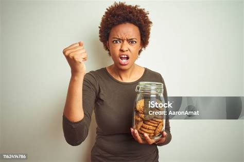 고립 된 배경에 초콜릿 칩 쿠키의 항아리를 들고 아프리카 계 미국인 여성은 화가 좌절 분노와 함께 소리 미친 고함 제기 손으로 고함 분노 개념 감정에 대한 스톡 사진 및