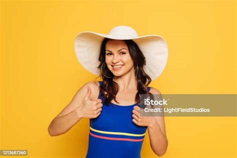 태양 모자와 수영복에 쾌활한 여자는 노란색에 고립 된 엄지 손가락을 보여주는 갈색 머리에 대한 스톡 사진 및 기타 이미지