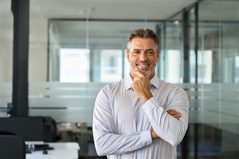 행복하고 자신감 있는 중년 사업가가 사무실에 서서 턱에 손을 얹고 생각한다 40 44세에 대한 스톡 사진 및 기타 이미지 40 44세 50 54세 경영자 Istock