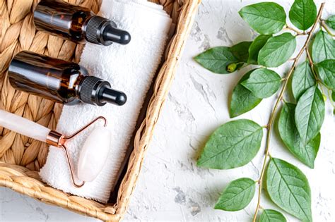 호박색 병에는 점적기 피펫이 있고 고리 버들 바구니에 석영 롤러가 있습니다 부드러운 일광이있는 콘크리트 배경 스킨 케어 세럼 또는 에센셜 오일 천연 화장품 얼굴 관리를 위한