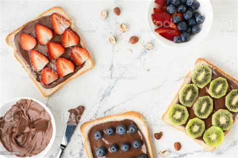 신선한 여름 딸기로 장식 된 초콜릿 헤이즐넛 스프레드를 곁들인 흰 빵 토스트 샌드위치의 상위 뷰 딸기 블루 베리 및 키위 과일 흰색 대리석 배경에 맛있는 아침 식사 빵에