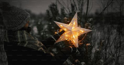 즐거운 성탄절 밤에 눈 덮인 겨울 공원의 소나무에 큰 조명 크리스마스 별을 두는 여자 마법의 겨울 시간 세련된 힙스터 여성 장식 크리스마스 트리 크리스마스 기적 사진