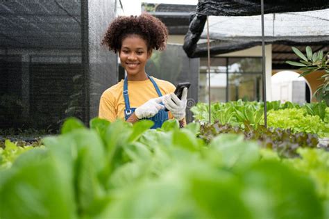 portrait of happy half thai half african woman farmer standing behind a vegetable plot and using