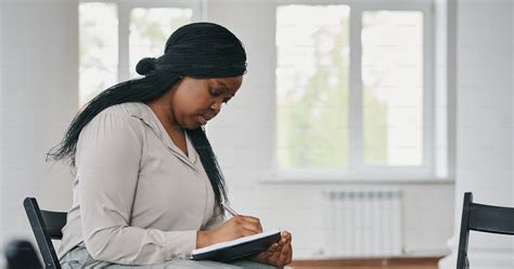 넓은 강의실에 앉아 심리 치료 세션 전후에 노트에 메모를 하는 젊은 진지한 흑인 여성 사진 Unsplash의 러시아 이미지