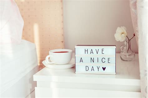 좋은 하루 문자 메시지를 조명된 상자 태양 빛에 머리 맡 테이블에 커피와 흰 꽃의 컵에 있다 좋은 아침 분위기입니다 환대 의료 서비스 개념입니다 선택적 초점입니다 공간에