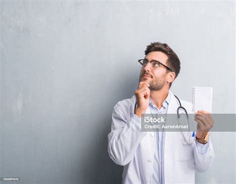 회색 그런 지 위에 잘생긴 젊은 의사 남자 벽 질문 매우 혼란 스 러 워 아이디어에 대해 빈 노트북 심각한 얼굴 생각 들고