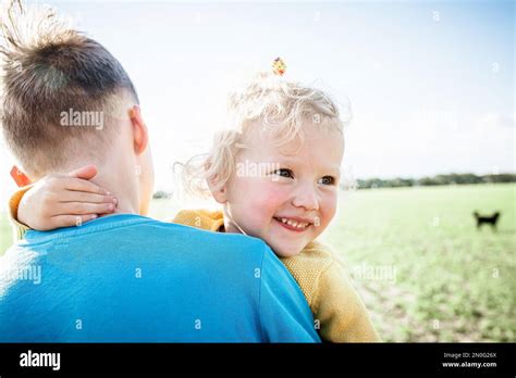 Little Sister Smiles Girl Looks Out From Behind Her Brothers Shoulder