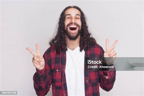 수염과 캐주얼 스타일에 검은 긴 곱슬 머리와 함께 행복 한 잘생긴 남자는 승리와 평화 서명 서 및 놀 얼굴로 카메라를 보고 빨간 셔츠 체크 무늬 4에 대한 스톡 사진 및