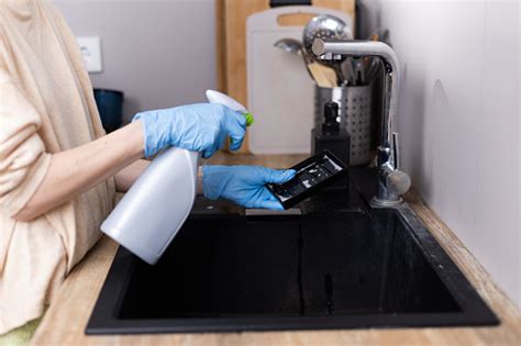 파란 장갑을 낀 사람현대적인 주방 환경에서 스프레이 병과 식기 홀더로 검은색 싱크대를 청소하고 가정 청소 루틴을 강조하고 위생을 유지합니다 가정 주방에 대한 스톡 사진 및