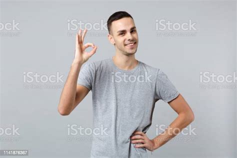 캐주얼에 서 있는 매력적인 젊은 남자의 초상화 카메라를 찾고 확인 제스처 회색 벽 배경에 고립 표시 사람들은 진심으로 감정