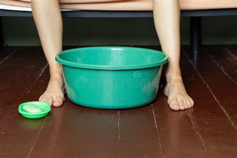 Girl Washes Her Feet In A Bowl Of Water On The Wooden Floor At Home