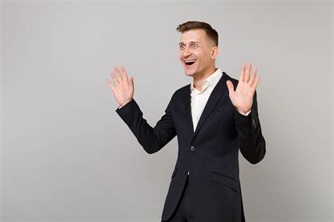 고전적인 검은 양복과 셔츠 스튜디오에 회색 벽 배경에 고립 손 확산 행복 젊은 사업가 흥분 성과 경력 부 비즈니스 개념입니다