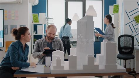 Man And Woman Analyzing Building Model And Maquette With Digital Tablet For Development Stock