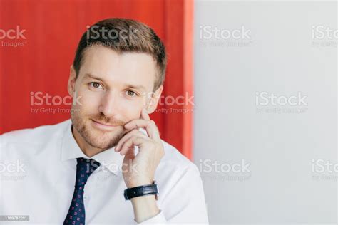 넥타이가달린 정장 흰색 셔츠를 입고 뺨에 손을 잡고 인생의 새로운 무대를 시작하고 빨간색과 흰색 배경을 배경으로 포즈를 취하는 남성 사무직 근로자를 안심시켰습니다 비즈니스