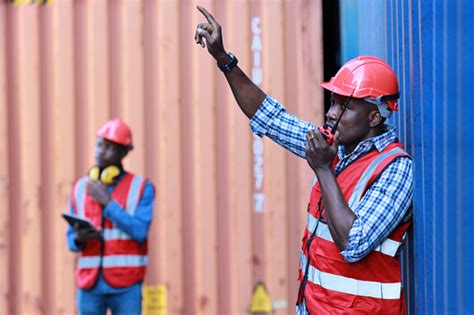 태블릿과 워키토키 무선 조종 적재 컨테이너 상자를 사용하는 감독 안전모를 쓴 엔지니어 또는 작업자는 컨테이너 화물 현장에서 작업하고 산업용 컨테이너 화물 화물선을 점검합니다