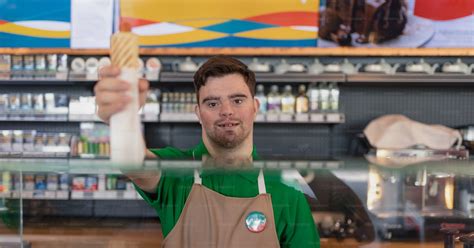 다운 증후군을 앓고있는 행복한 웨이터가 바게트를 제공하고 주유소의 카페에서 의상을 입었습니다 사진 Unsplash의