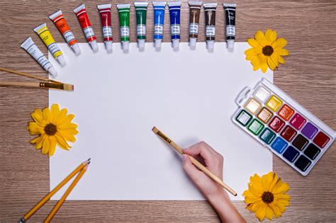 페인트 튜브와 빈 캔버스가 있는 예술가의 작업 공간 나무 테이블 위에 반원으로 배열된 생생한 페인트 튜브로 둘러싸인 빈 흰색 캔버스가 특징인 창의적인 작업 공간입니다 공란에