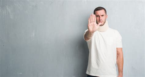 젊은 백인 남자가 심각 하 고 자신감 표현 방어 제스처 정지 표시를 하 고 오픈 손으로 목 칼라를 입고 회색 그런 지 벽 위로
