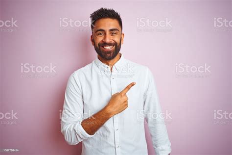 고립 된 분홍색 배경 에 서있는 우아한 셔츠를 입은 젊은 인도 사업가는 얼굴에 행복하고 자연스러운 표정으로 손과 손가락으로