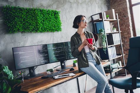 Focused Female Programmer In Casual Workspace Holding Coffee And Coding On Modern Computer In