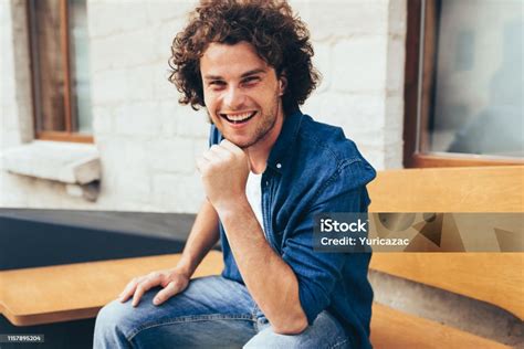 곱슬 머리를 가진 똑똑한 잘생긴 젊은 남자 카메라를보고 도시 거리에서 벤치에 앉아 야외에서 휴식을 취하는 행복한 남성 학생 사람과 라이프 스타일 개념 남자에 대한 스톡 사진