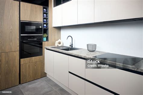 인덕션 스토브 호브 밥솥 싱크대 전자레인지 오븐 냉장고 식기 세척기와 같은 빌트인 가전제품이 있는 나무 외관과 석기 조리대의