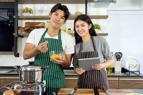 귀여운 해피 커플의 초상화 셀 카 액션에 앞치마를 들고 태블릿 및 시리얼을 준비 하 고 현대 부엌에서 아침을 요리 하 고 즐거운 시간을 보내고 2명에 대한 스톡 사진 및