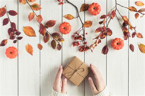 흰색 복고풍 나무 보드에 크래프트 종이 상자에 선물을 포장 하는 여자 나뭇잎 로완 과 작은 호박 추수 감사절 가을 가을 컨셉