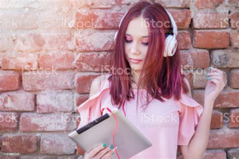 벽돌 벽 야외에 대 한 헤드폰으로 디지털 태블릿에 음악을 듣고 귀여운 빨간 머리 소녀 갈색 머리에 대한 스톡 사진 및 기타