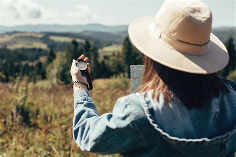 화창한 산에서 여행지도와 나침반을 들고 세련된 힙스터 소녀 여름 방학에 산 꼭대기에서 지도를 탐험하고 하이킹을하는 모자를 쓴 여성 방랑자 및 여행 개념 나침반에 대한 스톡