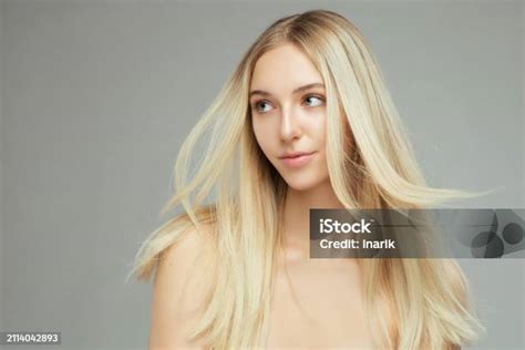 긴 실크 머리를 가진 아름 다운 금발 소녀 금발의 부드러운 헤어 스타일을 가진 뷰티 모델은 회색 배경 위에 바람을 흔들고