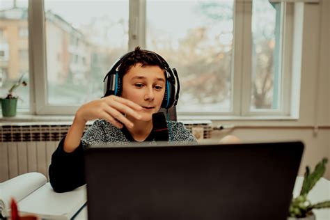 집에서 온라인 수업에 참석하는 소년 교사 및 학교 친구들과 연결하기 위해 노트북과 헤드셋을 사용하는 어린이 격리 중 학교 교육 및 사회적 거리 매스컴에 대한 스톡 사진 및