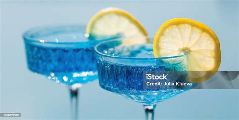 맛있는 블루 칵테일 블루 라군과 수영장 배경에 노란색 레몬 한 잔 알코올 칵테일 Curacao 리큐어 얼음 조각 및 레몬 조각을 곁들인 육즙이 많은 과일 파란색 0명에 대한