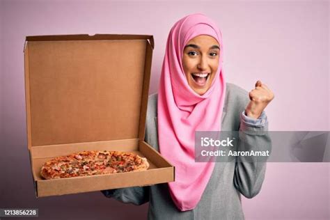 젊은 아름다운 아랍 여자 핑크 무슬림 히잡을 입고 배달 상자를 들고 이탈리아 피자 자랑과 승리와 성공을 축하 매우 흥분 응원 감정 감정에 대한 스톡 사진 및 기타 이미지