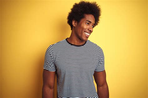 해군 스트라이프 티셔츠를 입고 고립된 노란색 배경 위에 아프로 머리를 한 아프리카 계 미국인 남성이 얼굴에 미소를 지으며 옆으로 바라보고 자연스러운 표정 자신감 있게 웃고