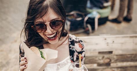 육즙이 많은 버거와 레모네이드를 들고 먹는 세련된 힙스터 여성 햄버거를 물고 재미있고 길거리 음식 축제에서 웃고 있는 보호 소녀 여름철 여름 방학 피크닉 텍스트를