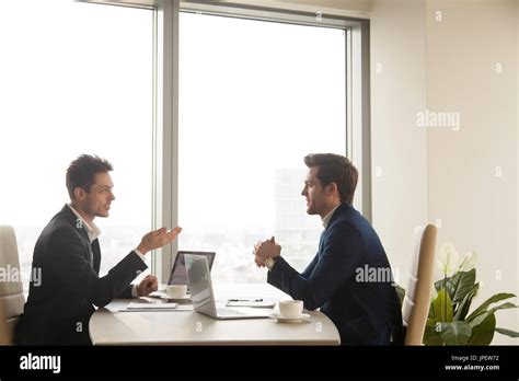 Business Meeting Of Two Partners Talking And Working On Laptops Stock