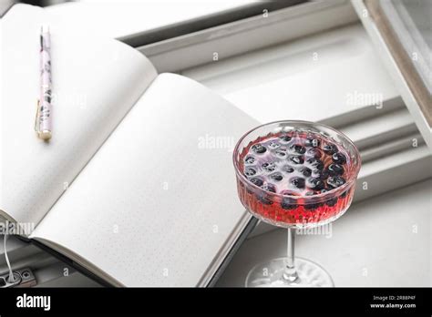 An Open Notebook With Blank Pages And A Glass Of Red Cocktail With