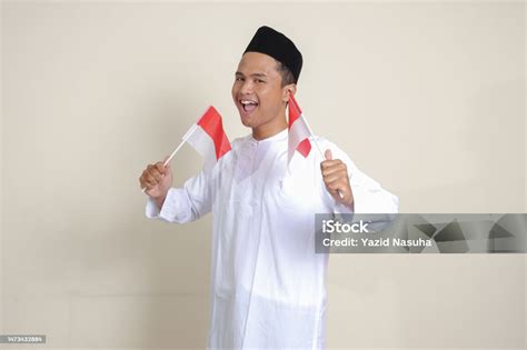 해골 모자를 쓴 매력적인 아시아 무슬림 남자의 초상화는 인도네시아 국기를 들고 주먹을 들고 성공을 축하합니다 회색 배경에 격리된 이미지 20 24세에 대한 스톡 사진 및