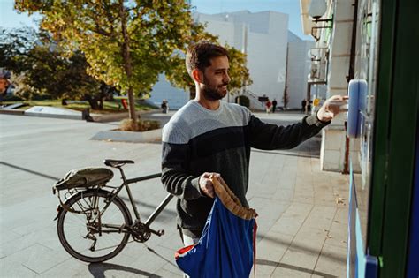 젊은 남자가 자전거를 타고 햇볕이 잘 드는 도시 거리의 야외 재활용 기계에서 플라스틱 병을 재활용합니다 25 29세에 대한 스톡 사진 및 기타 이미지 Istock
